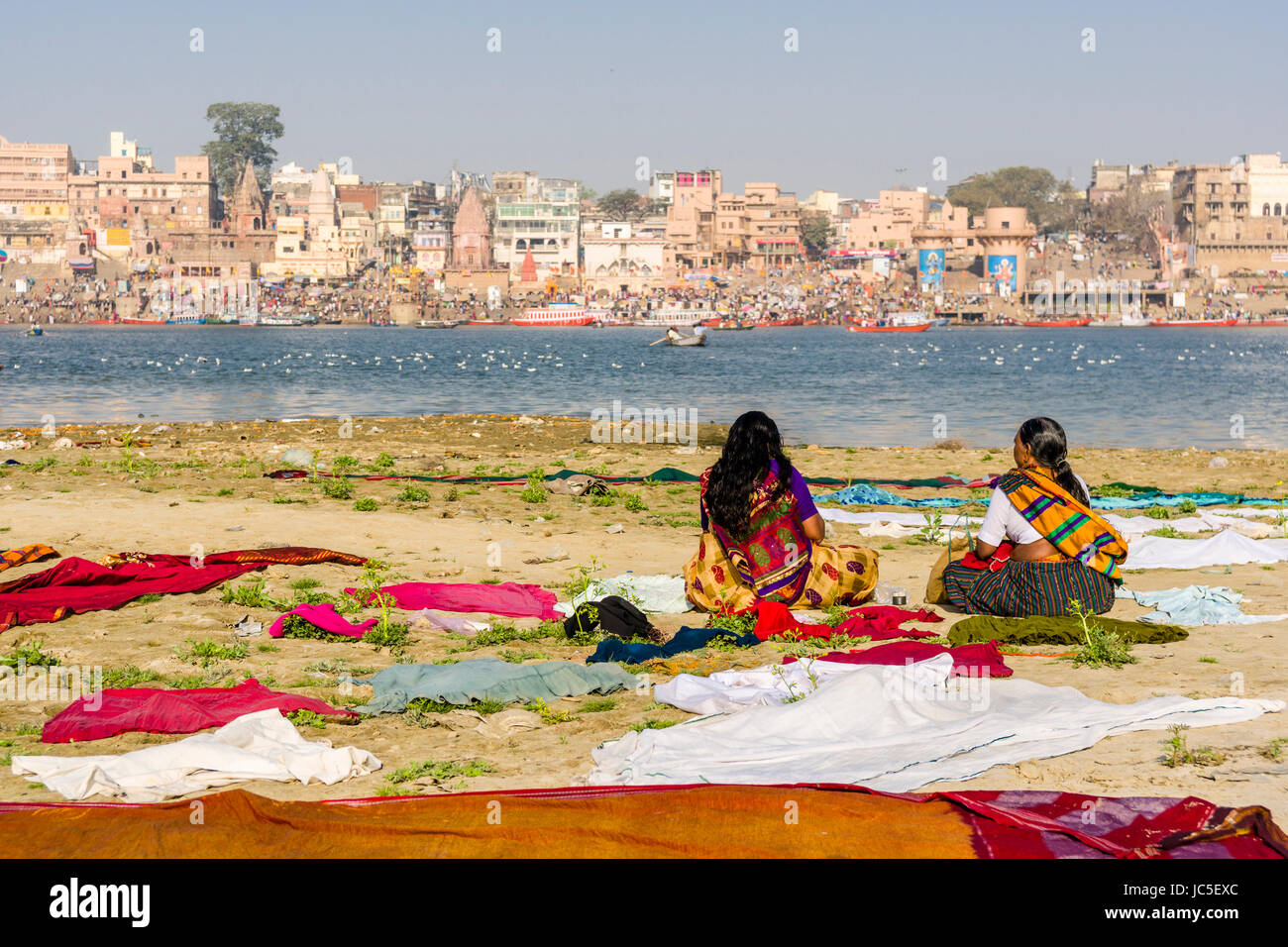 Two women are sitting on the sand banks at the holy river Ganges ...