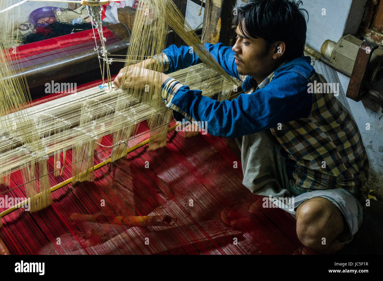 A man is weaving silk material at a old fashion handloom in a factory ...