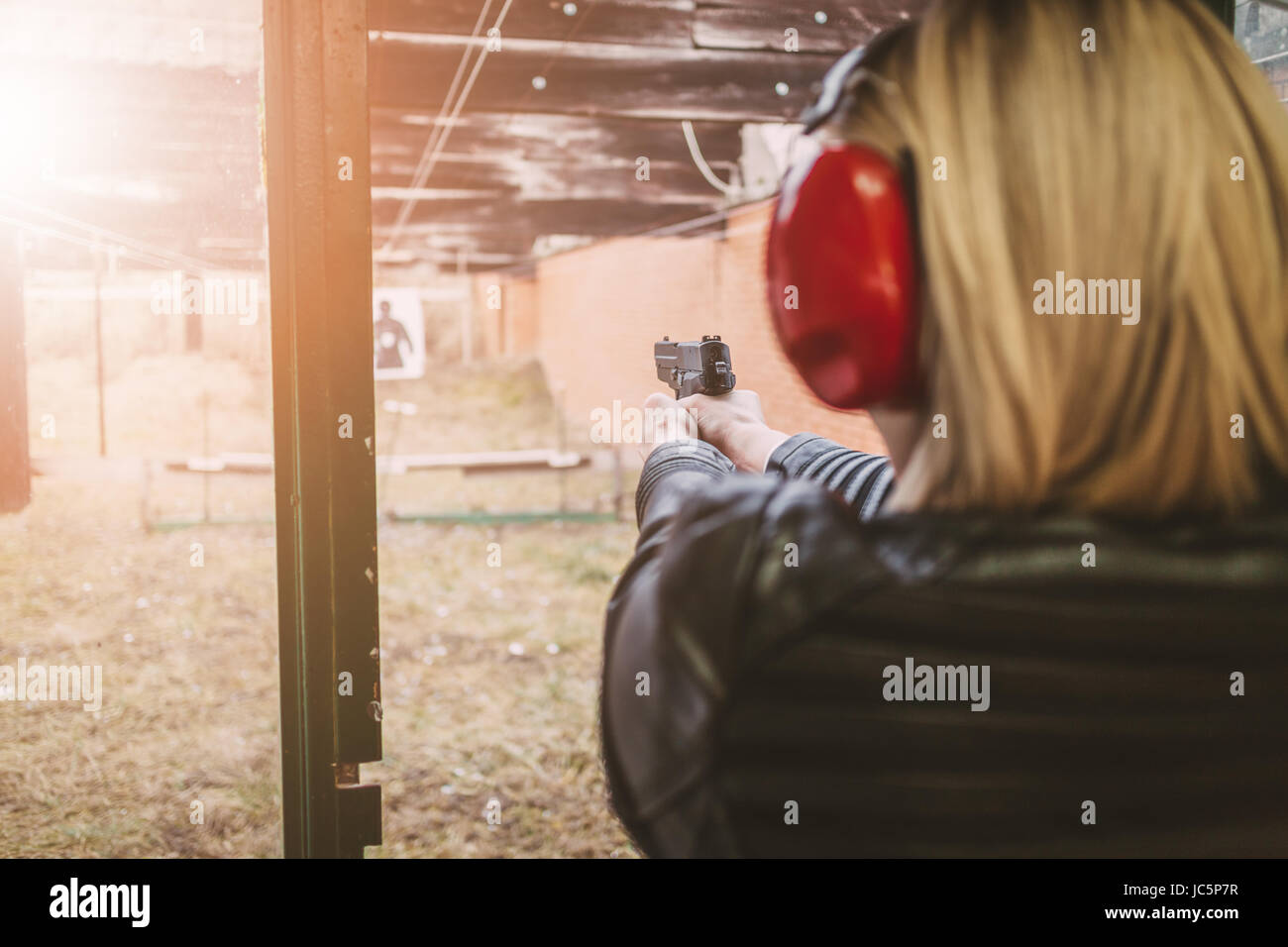 Woman firing with pistol on target at the shooting range. Rear view ...
