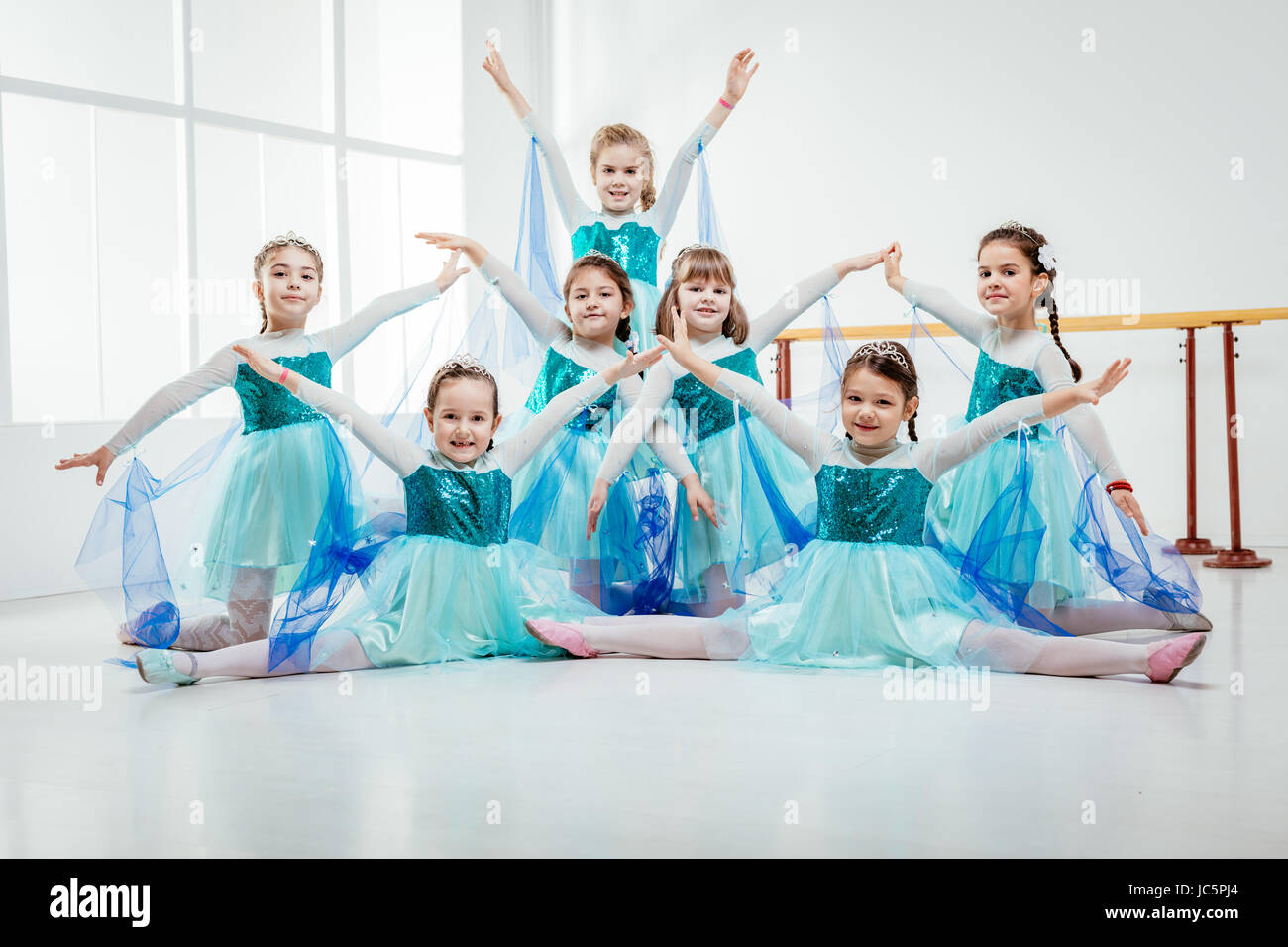 Smiling little girls in dresses practicing postures during ballet class ...