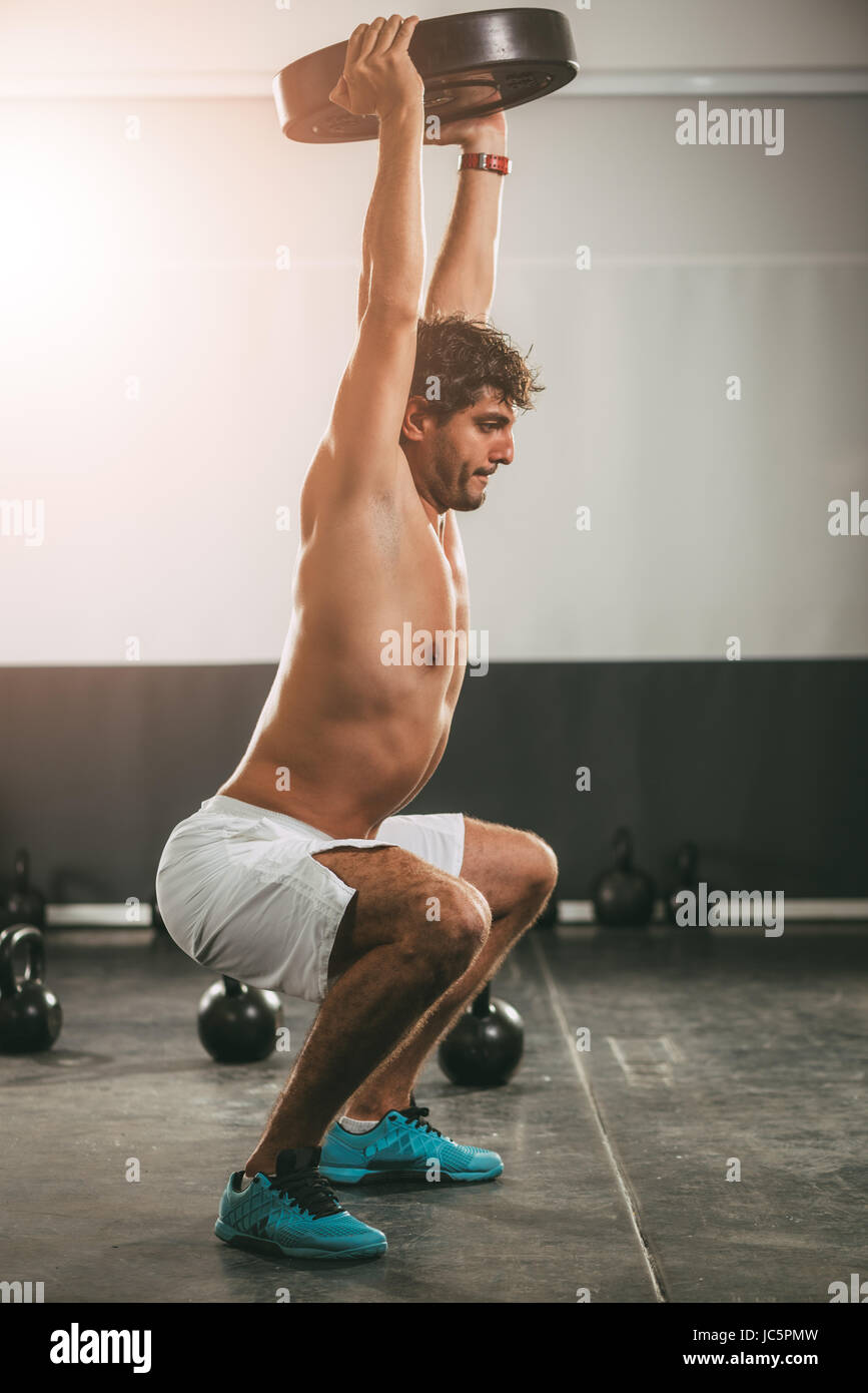 Young muscular man doing squats exercise with dumbbell. Strong male ...