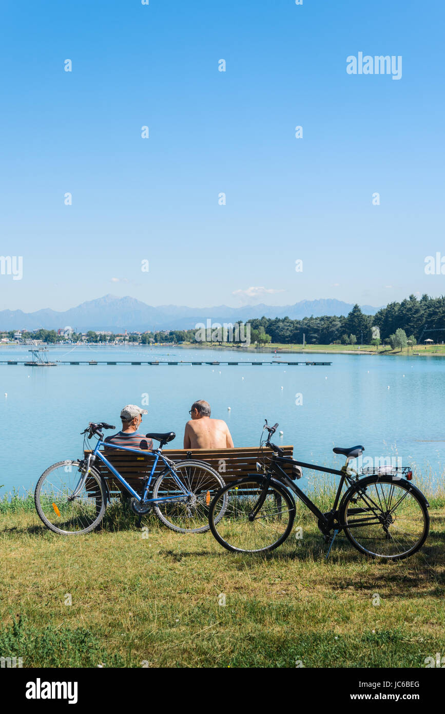 Two elderly men sit on a park bench after biking in Idroscalo, Milan ...