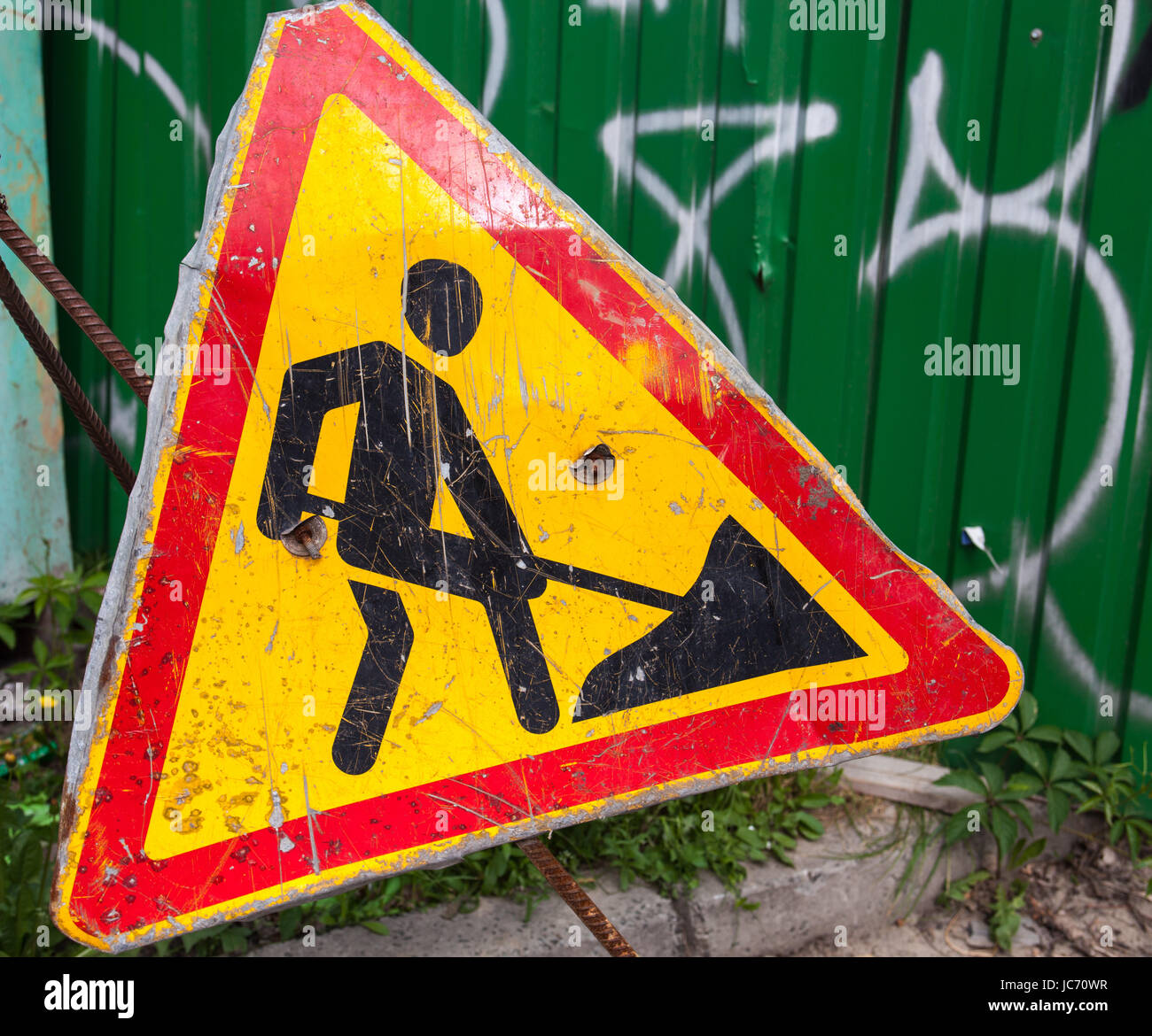 Old scratched metal roadworks sign near the green fence Stock Photo - Alamy