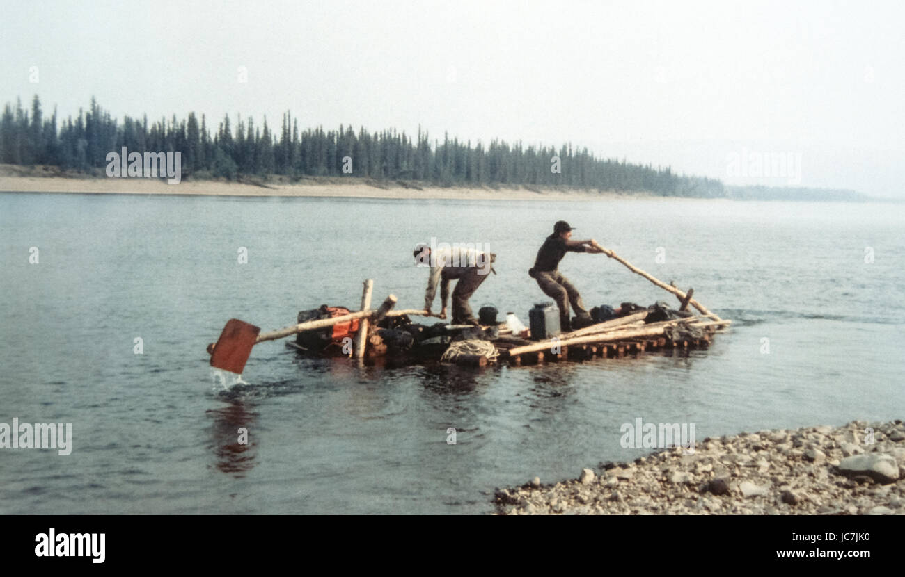 Two men rowing down the riveron self-made log raft. Vintage expedition ...