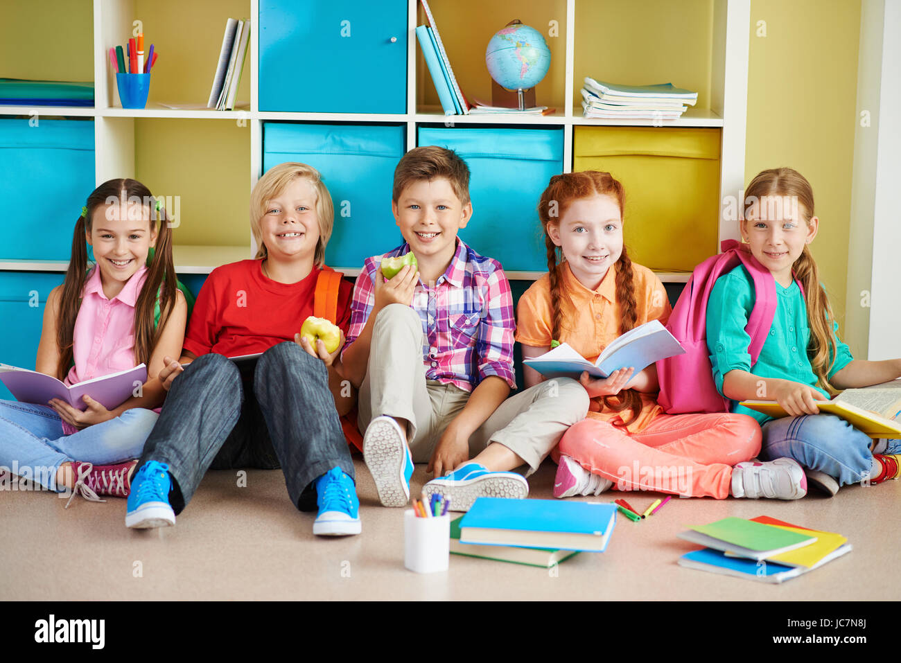 Cute friends sitting on the floor of classroom and doing schoolwork ...