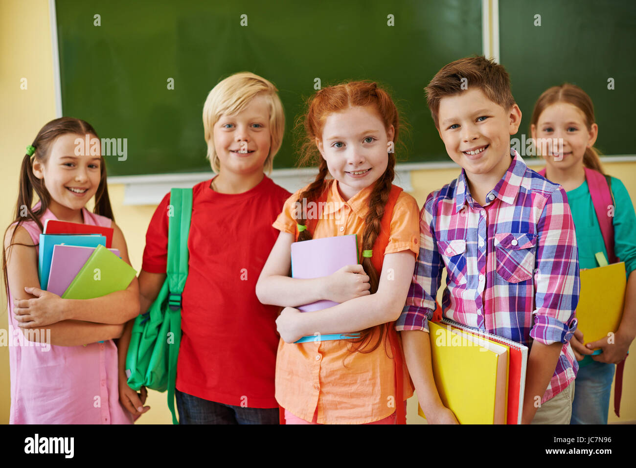 Five friendly classmates looking at camera on background of blackboard ...