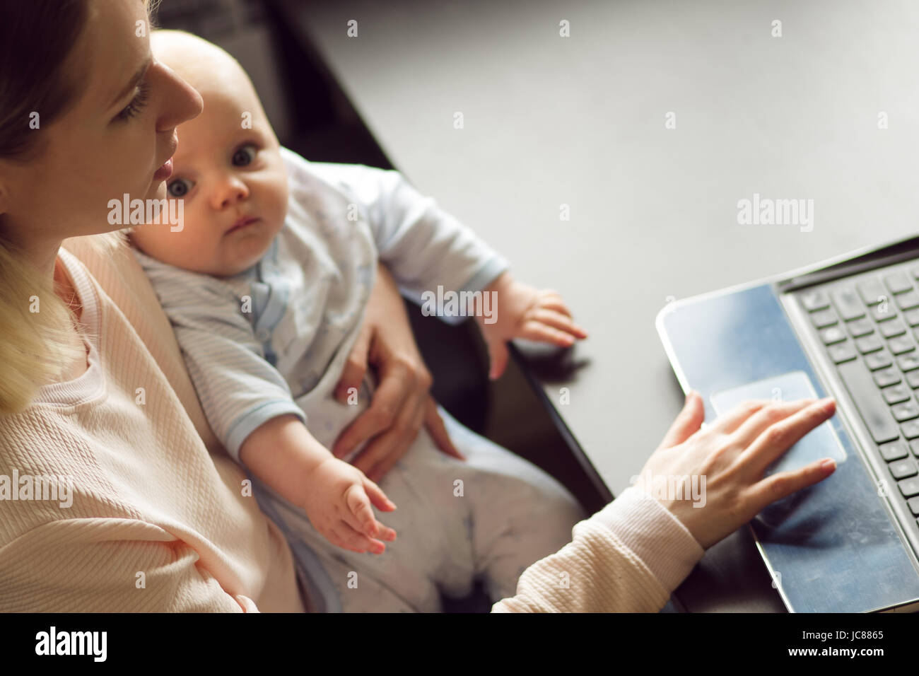 Young mother in home office with computer and her baby. Work and child ...