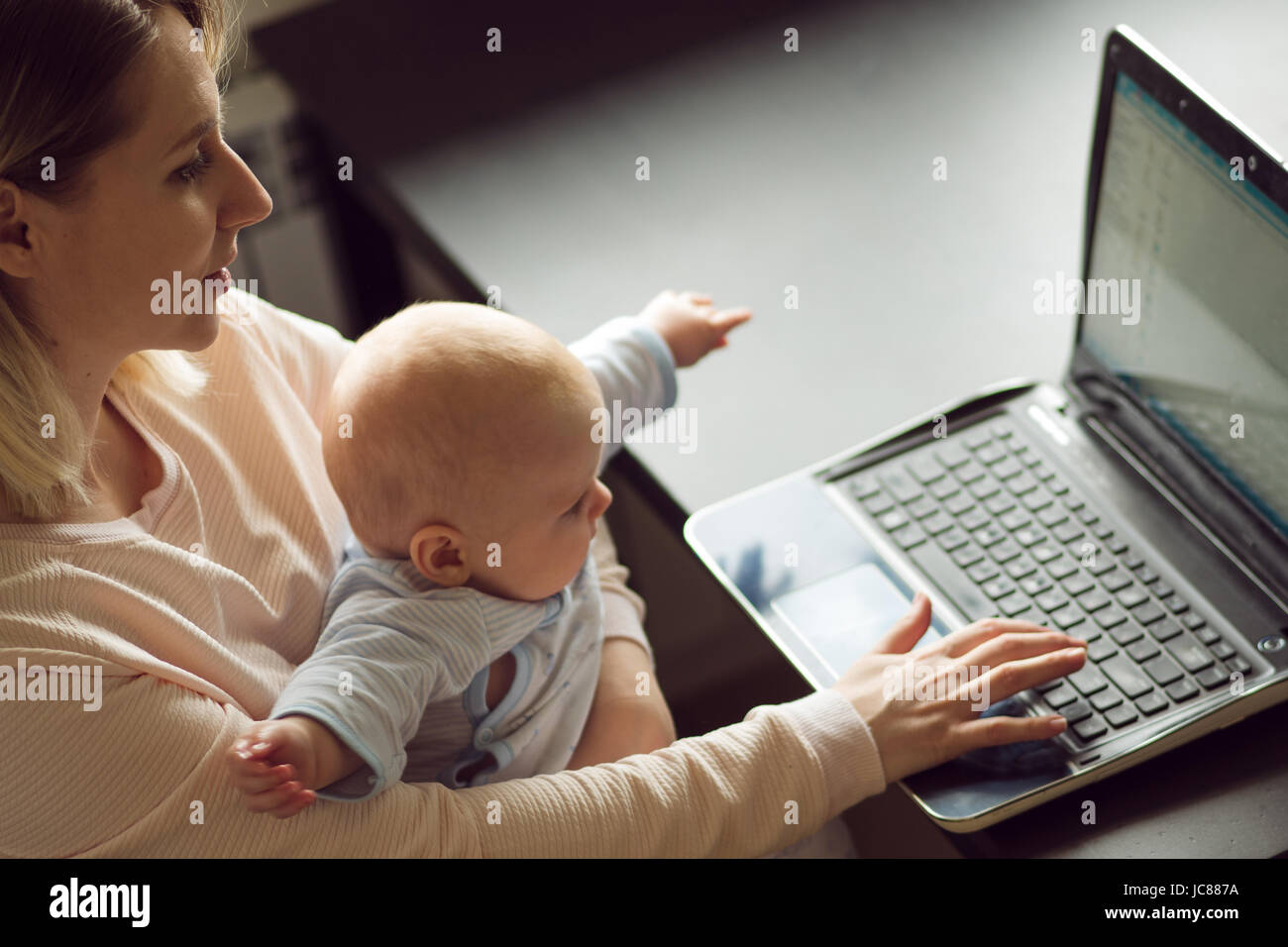 Young mother in home office with computer and her baby. Work and child ...