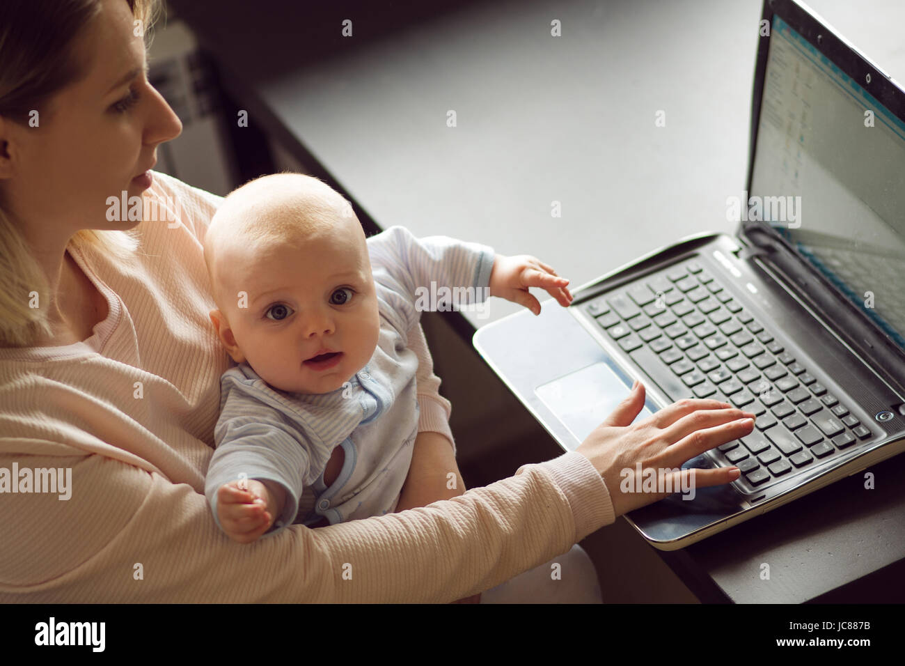 Young mother in home office with computer and her baby. Work and child ...