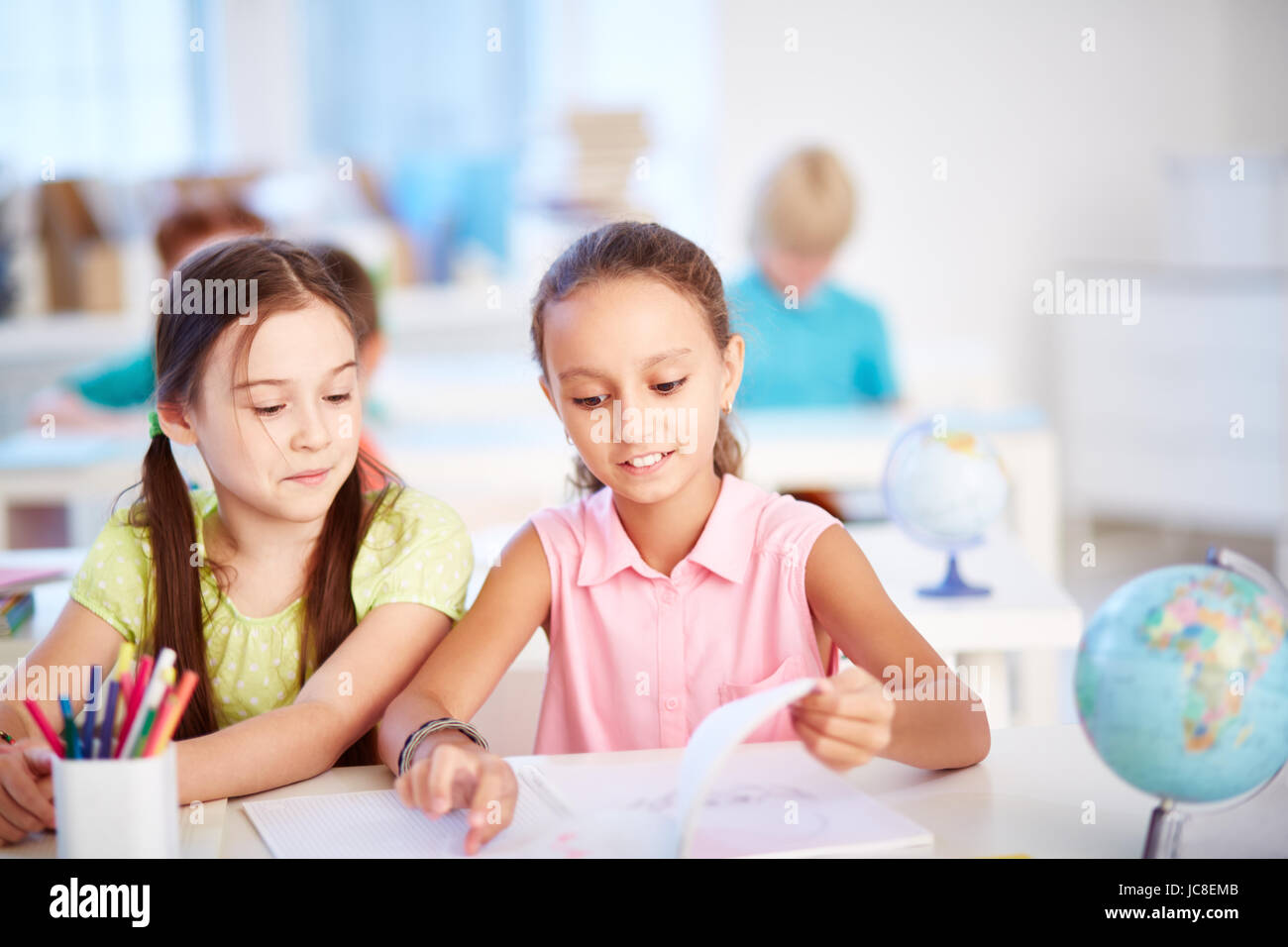 Two pretty friends discussing something in copybook at lesson Stock ...