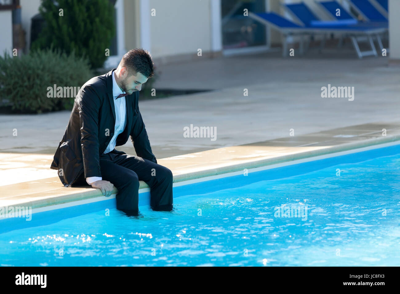 Man sitting by the pool, wearing black suit feeling sad and ...