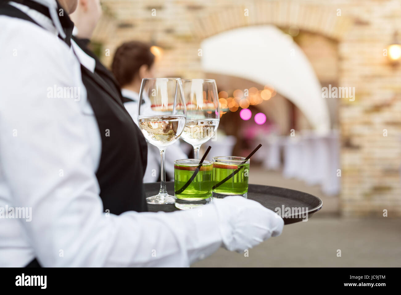 Midsection of professional waiters in uniform serving wine, cocktails ...