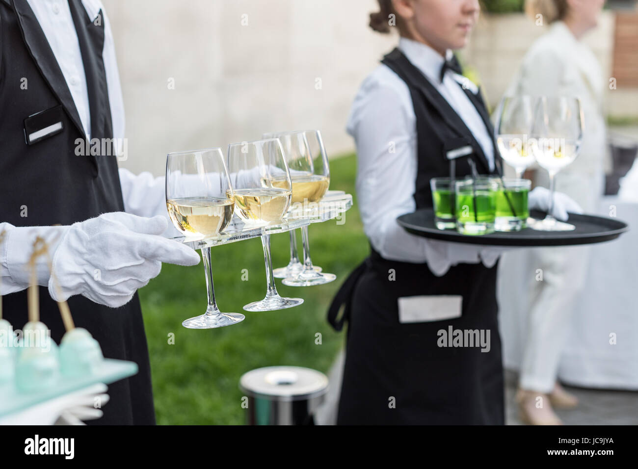 Midsection of professional waiters in uniform serving wine and snacks ...
