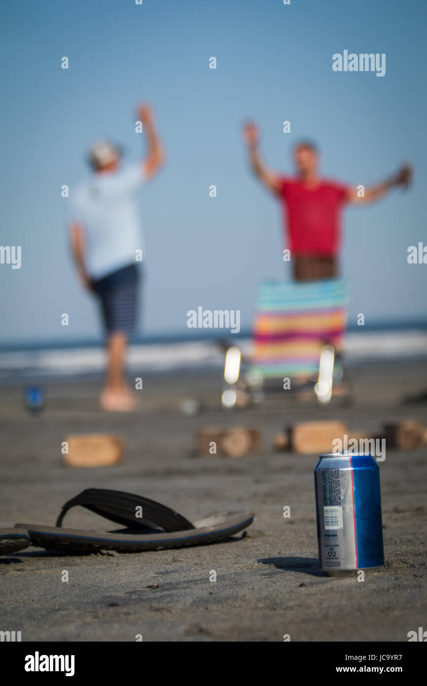 Two men cheering in the background of closeup of sandals and a can of ...
