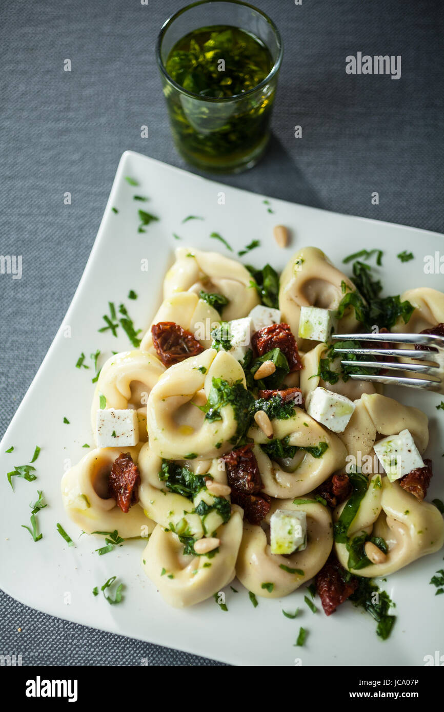 View from above of a stylish white plate with tortellini pasta, basil pesto and feta cheese ...