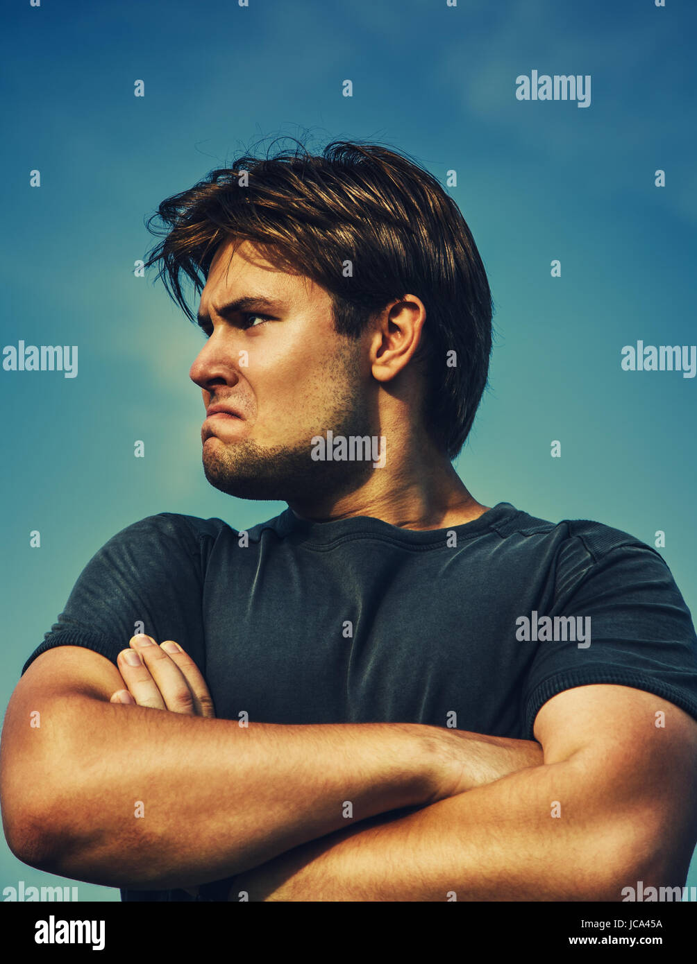 Big strong and very angry man portrait looking aside. On blue sky ...
