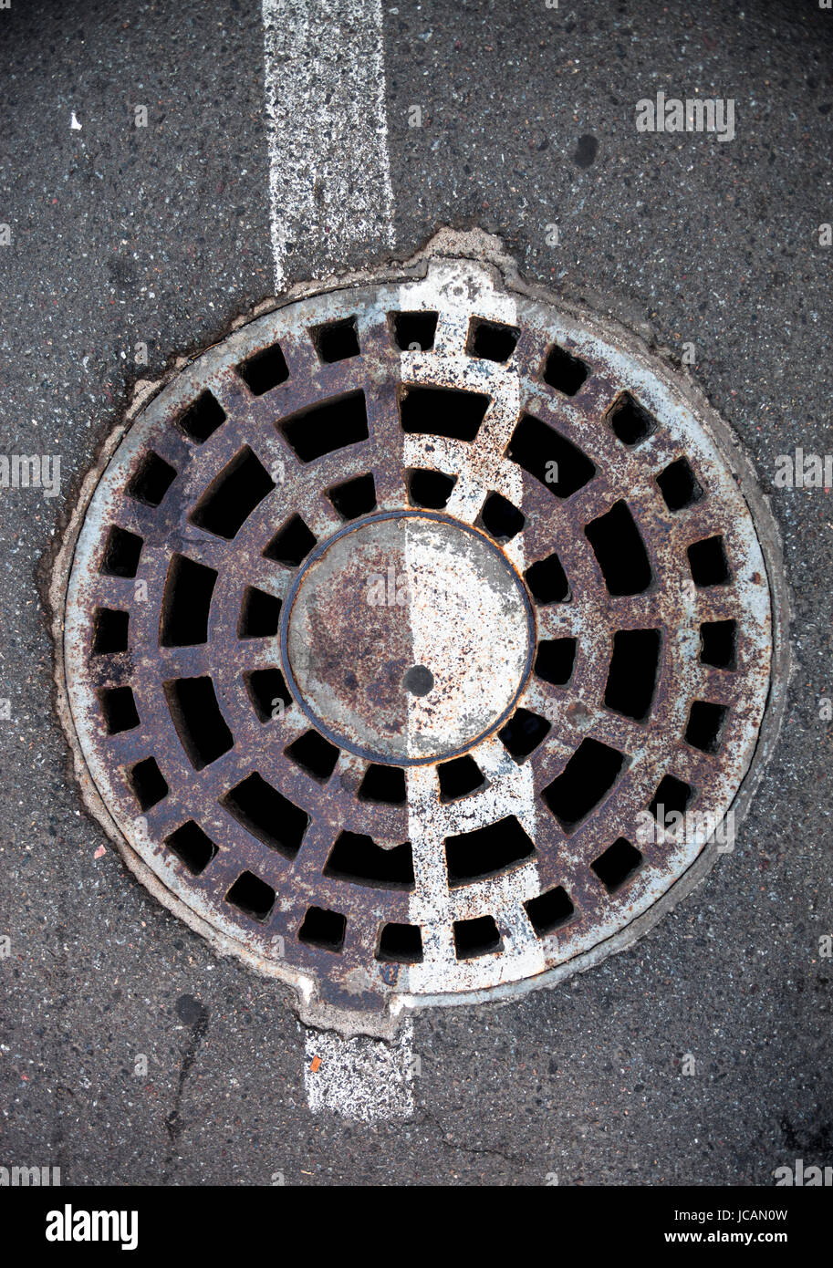 Manhole with metal cover in asphalt with white road marking line on it ...