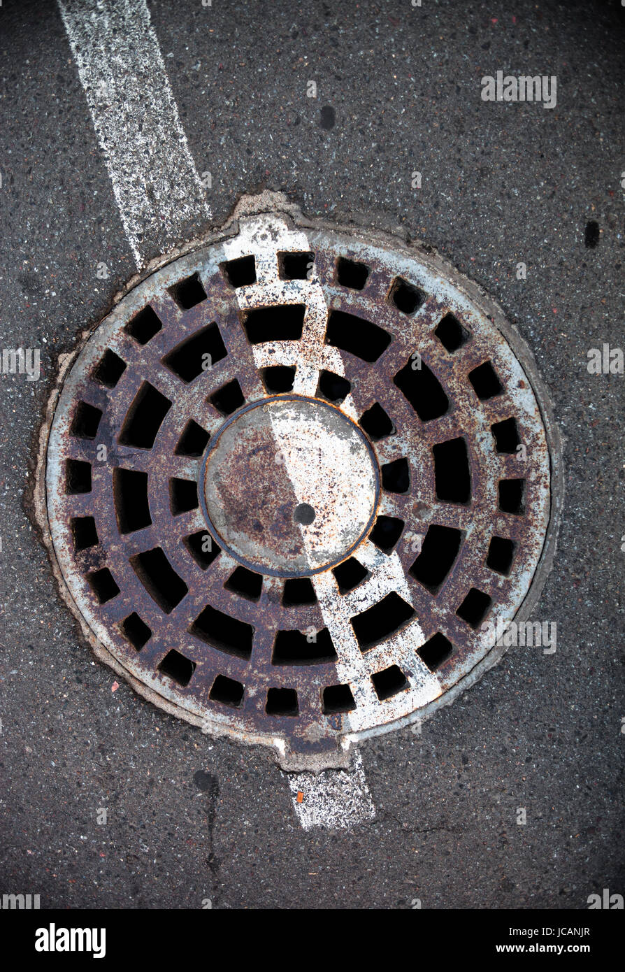 Manhole with metal cover in asphalt with white road marking line on it ...