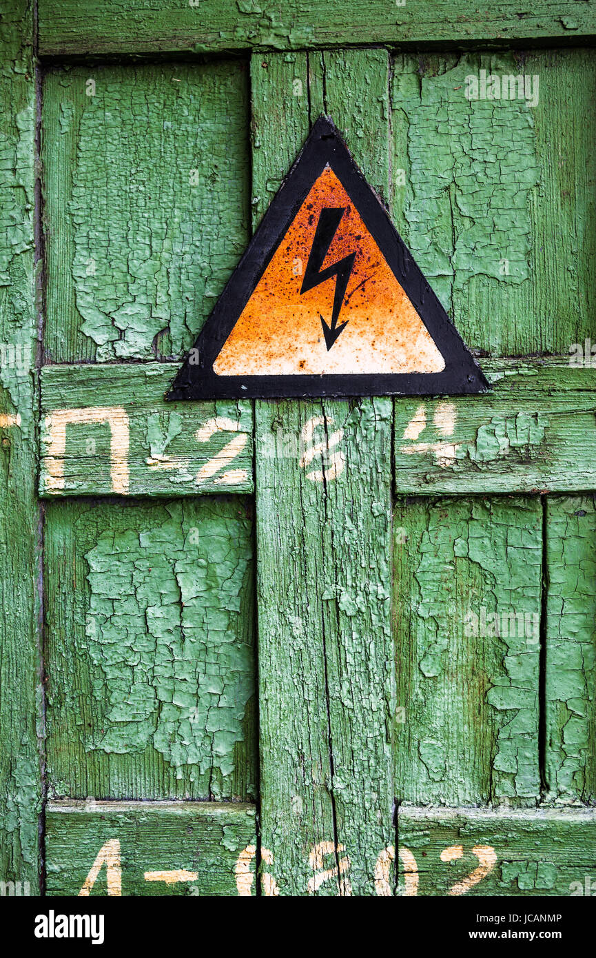 Old rusty warning high voltage sign on cracked green wooden surface ...