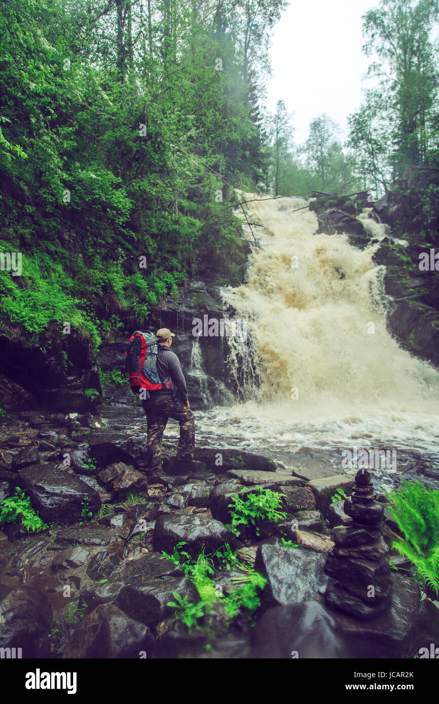 Traveler with a backpack near waterfall. It's raining Stock Photo - Alamy