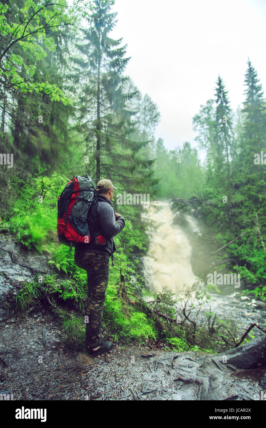 Traveler with a backpack near waterfall. It's raining Stock Photo - Alamy