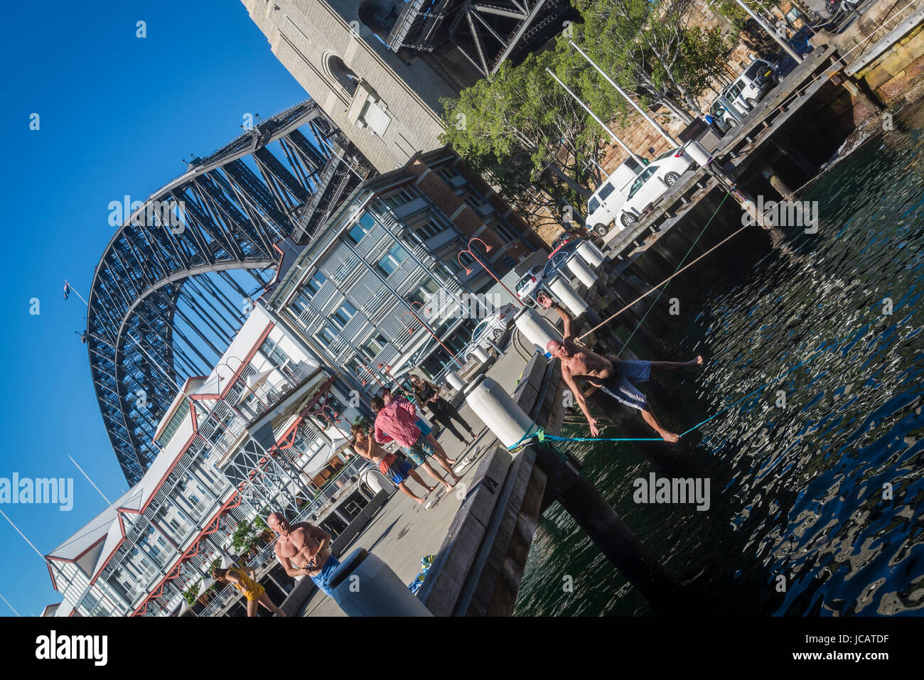 Man walking on rope in Walsh Bay with Harbour Bridge behind, also ...