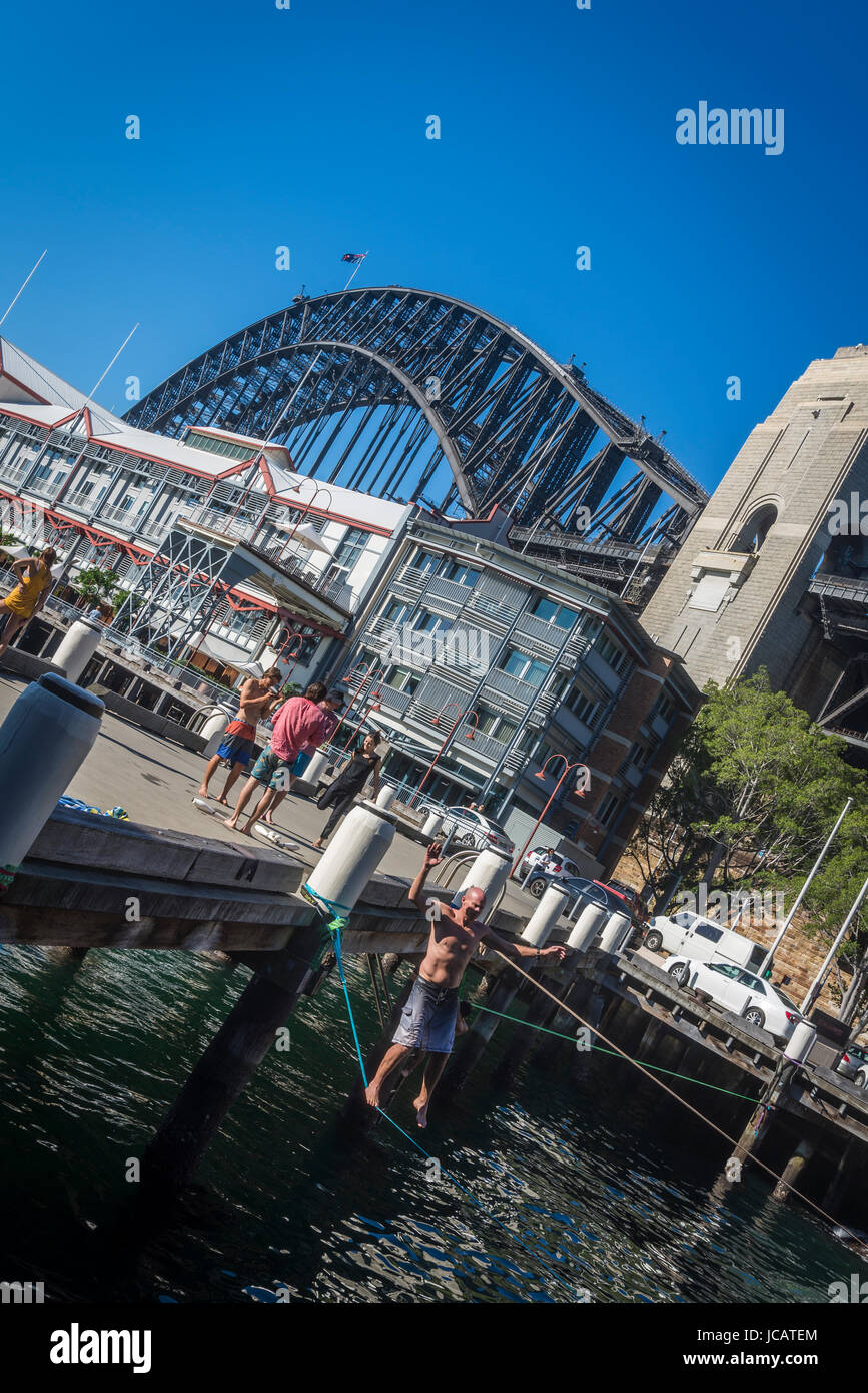 Man walking on rope in Walsh Bay with Harbour Bridge behind, also ...
