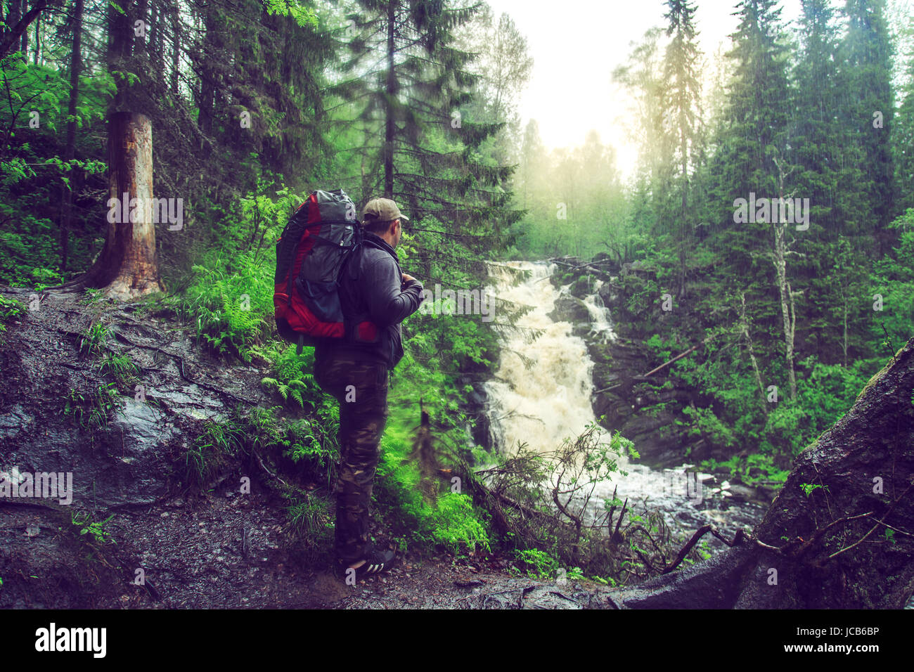 Traveler with a backpack near waterfall. It's raining Stock Photo - Alamy
