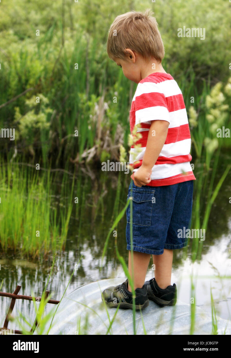 A happy two year old boy sparks curiousity at a nearby culvert while ...