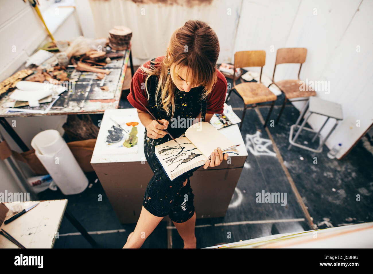 Female artist drawing pictures in her workshop. Young woman sitting and ...