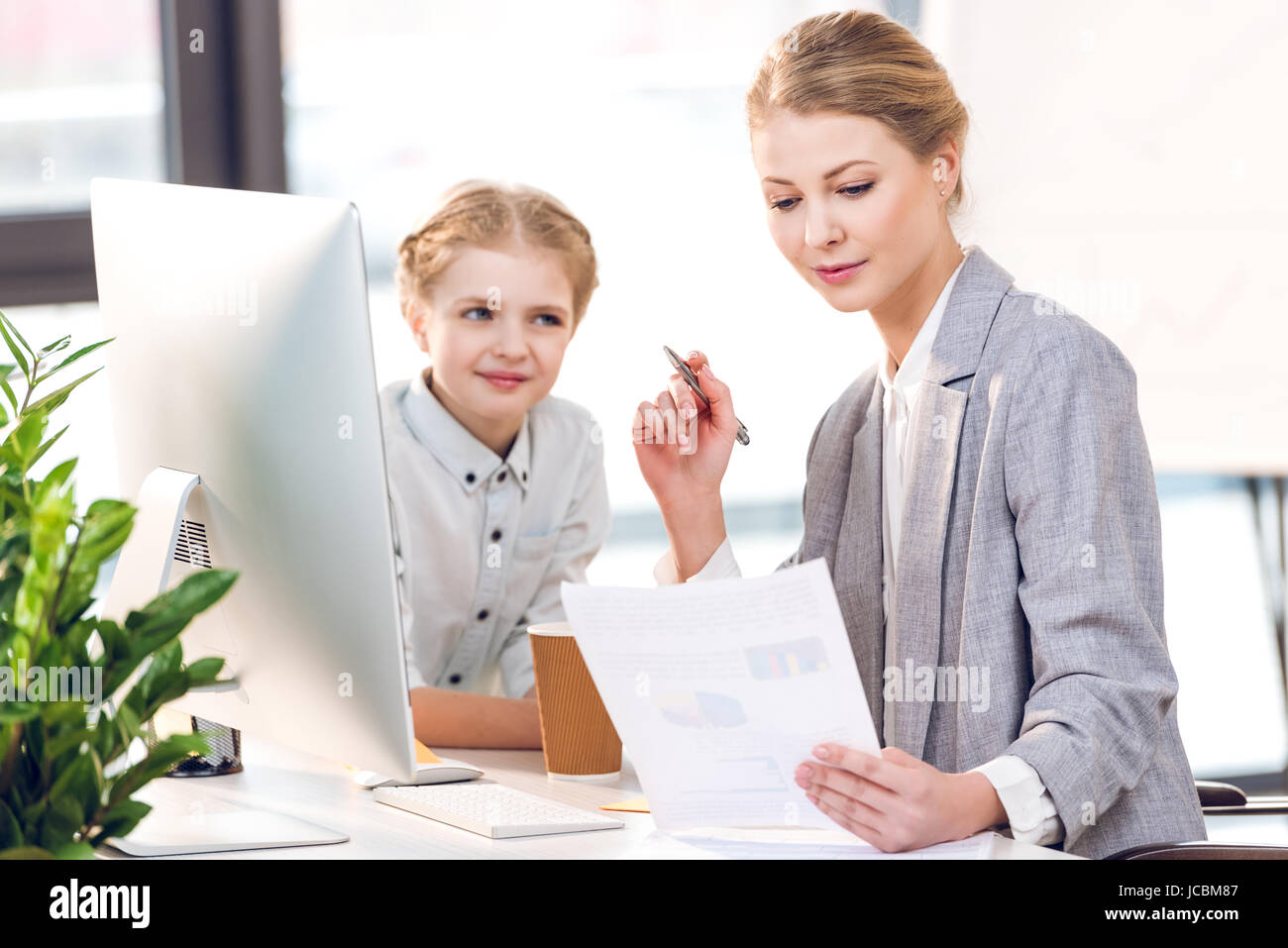 young mother working with computer and documents while daughter looking ...