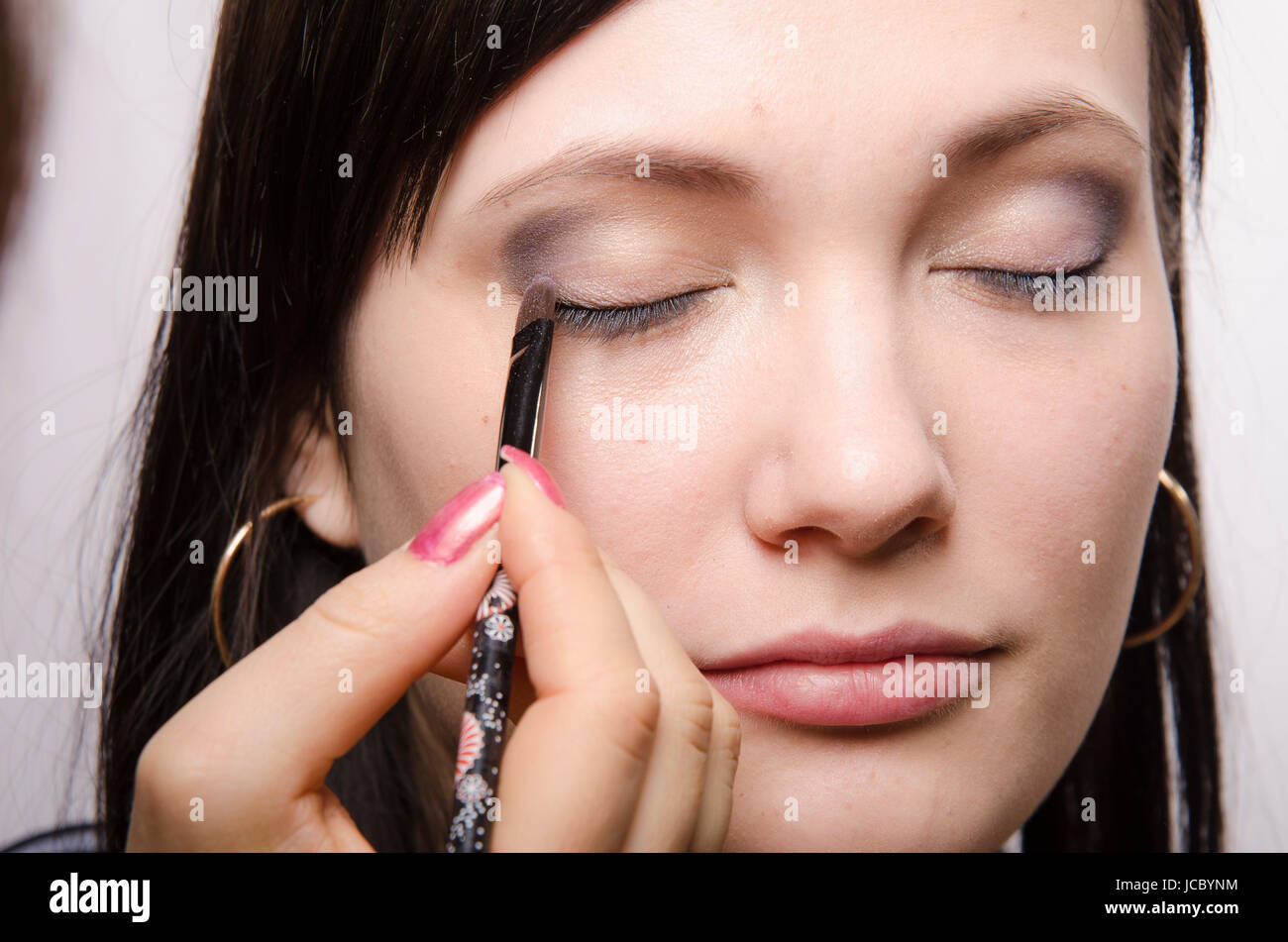 Makeup artist deals makeup on the model's face. She paints the shadows ...