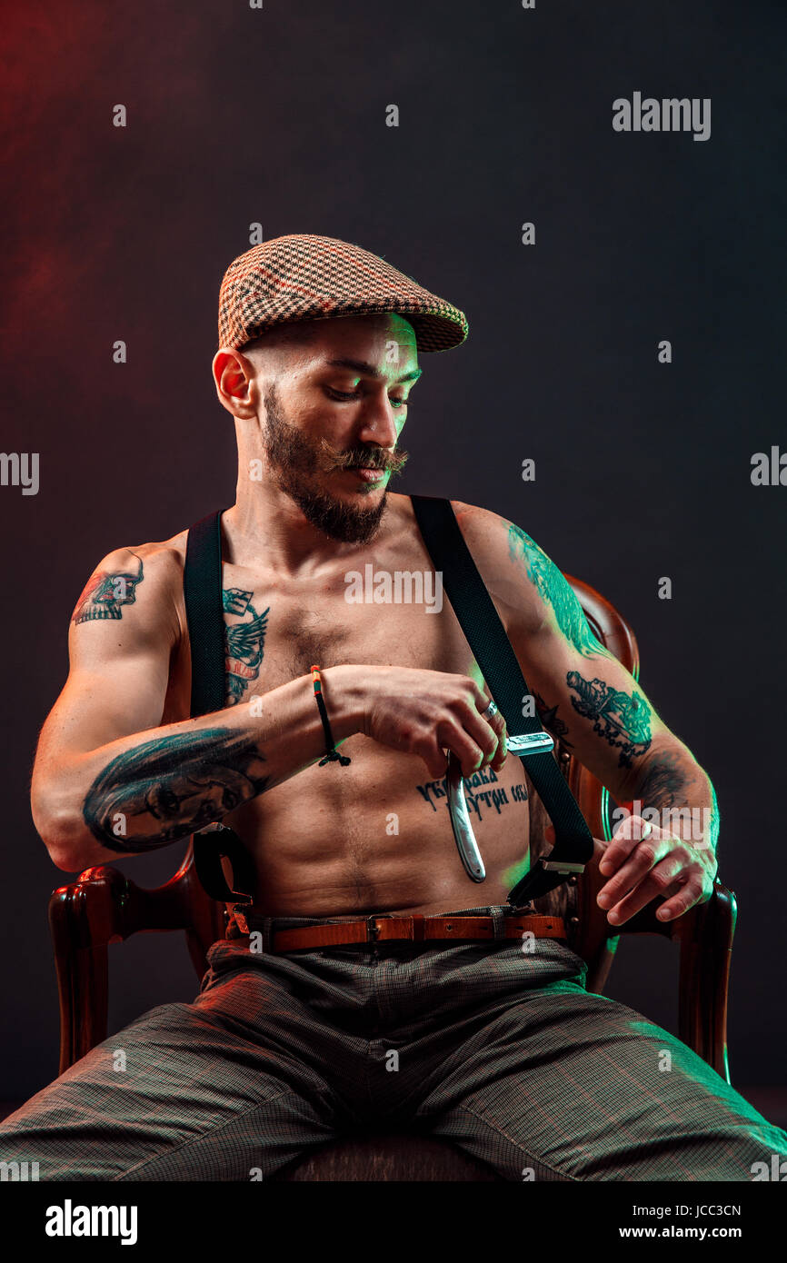 Stylish tattooed shirtless barber gangsta man with razor looking at ...