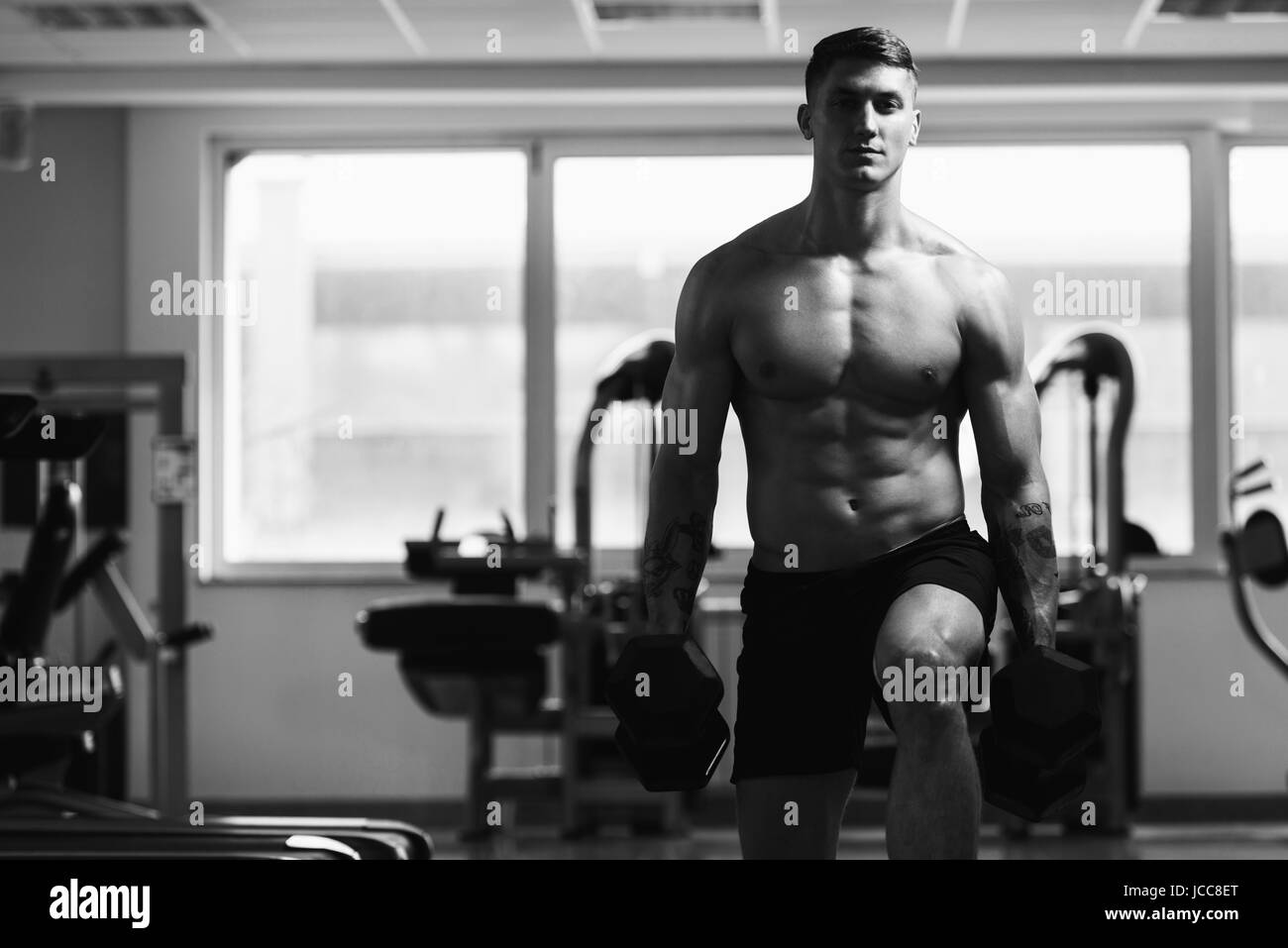 Young Man Working Out Legs With Dumbbells In A Gym - Squat Exercise ...