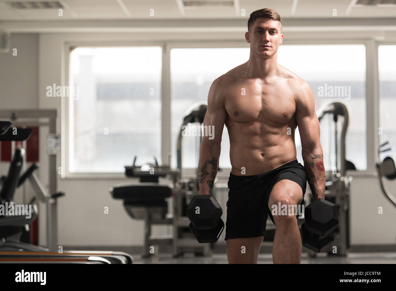 Young Man Working Out Legs With Dumbbells In A Gym - Squat Exercise ...