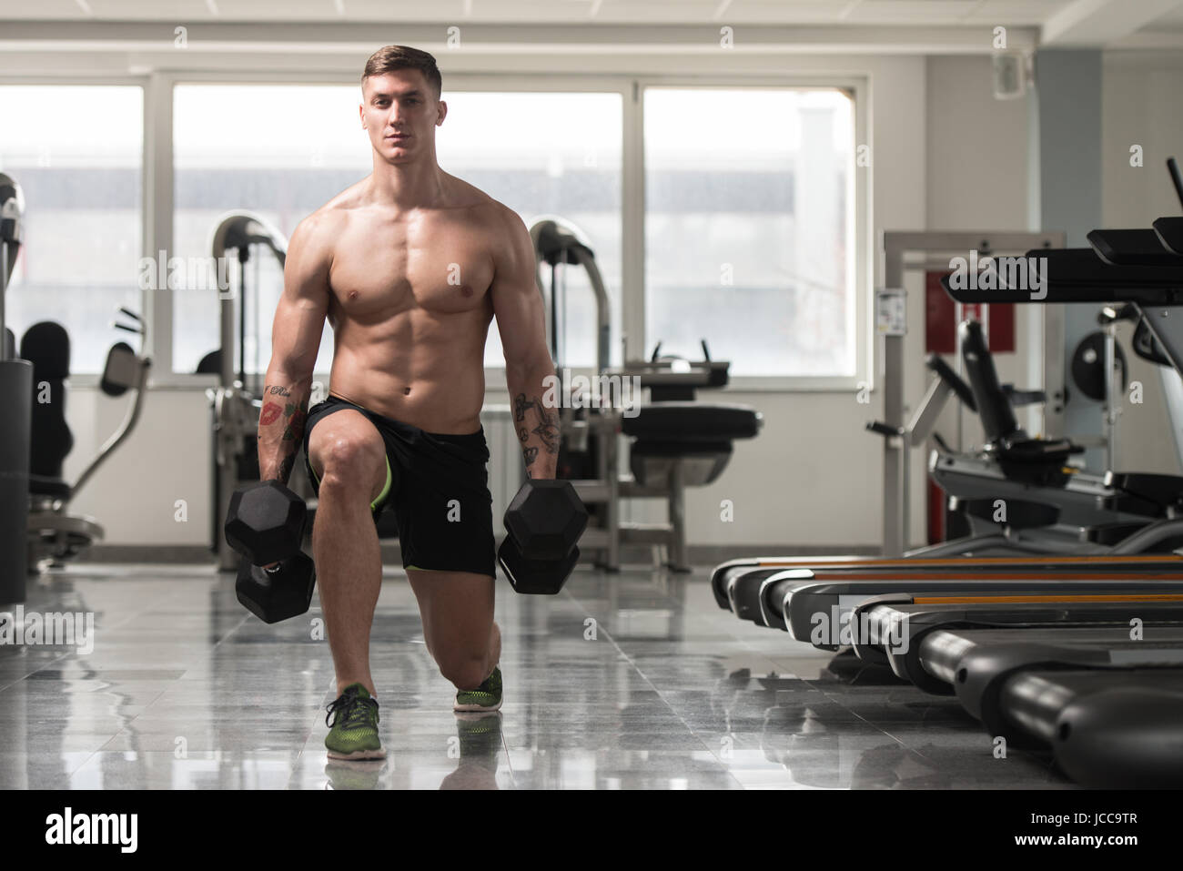 Healthy Fitness Man Working Out Legs With Dumbbells In A Gym - Front ...