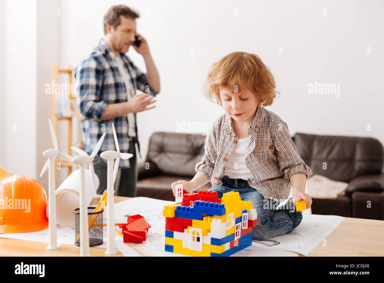 Positive delighted child sitting on the table while making toy house ...
