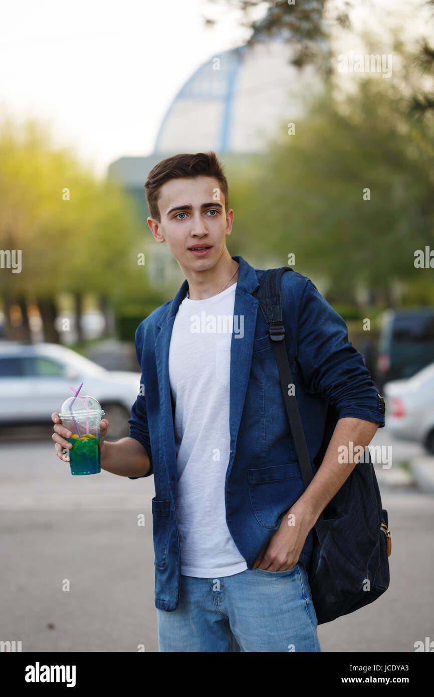 A young guy holding a glass of fruit fresh. He is wearing a jacket, a ...