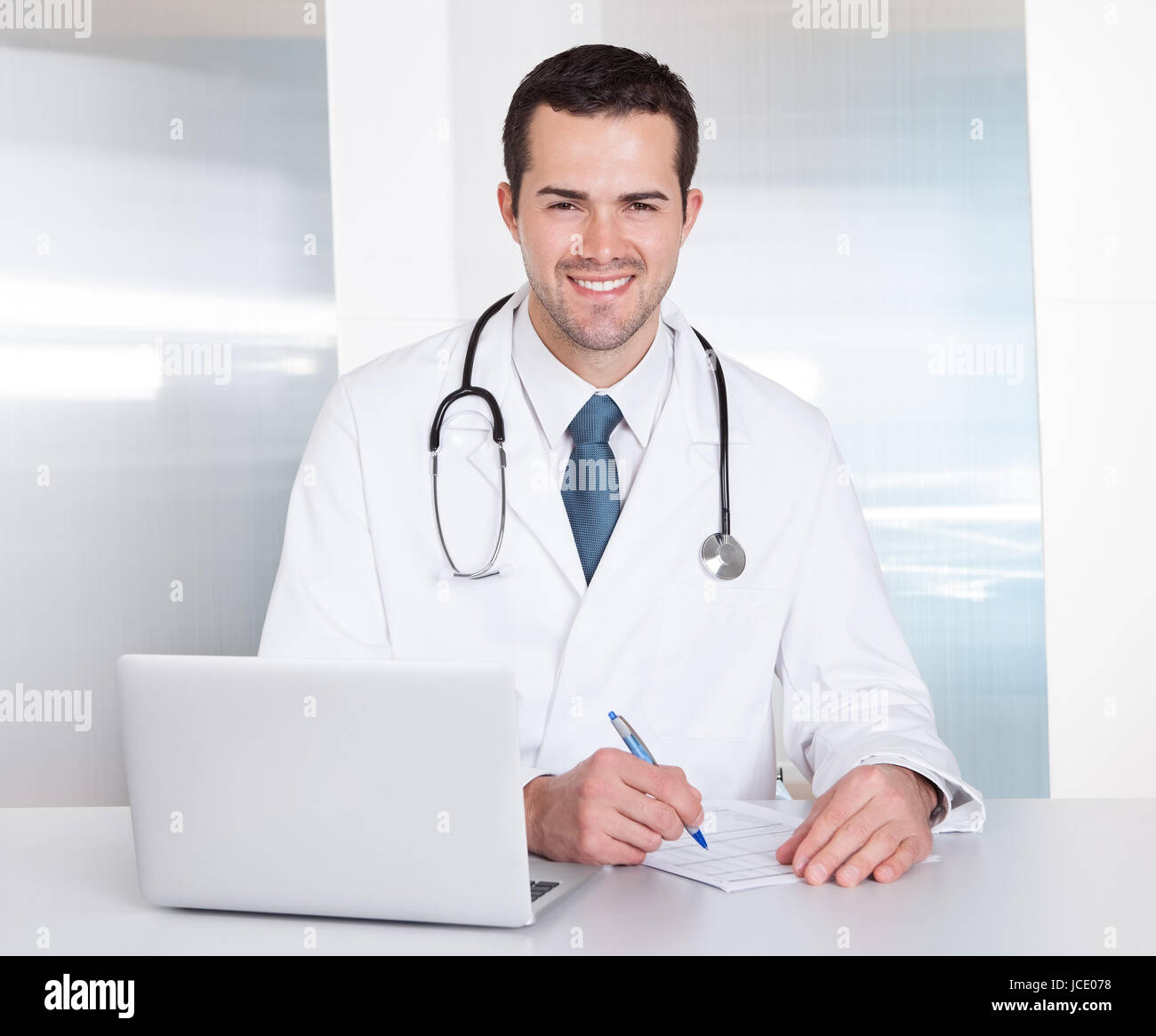Portrait of cheerful doctor sitting at the desk working on laptop Stock ...