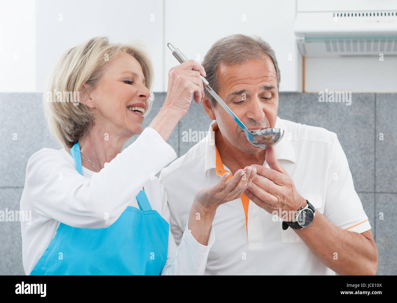 Woman Making His Husband To Taste The Food In Kitchen Stock Photo - Alamy