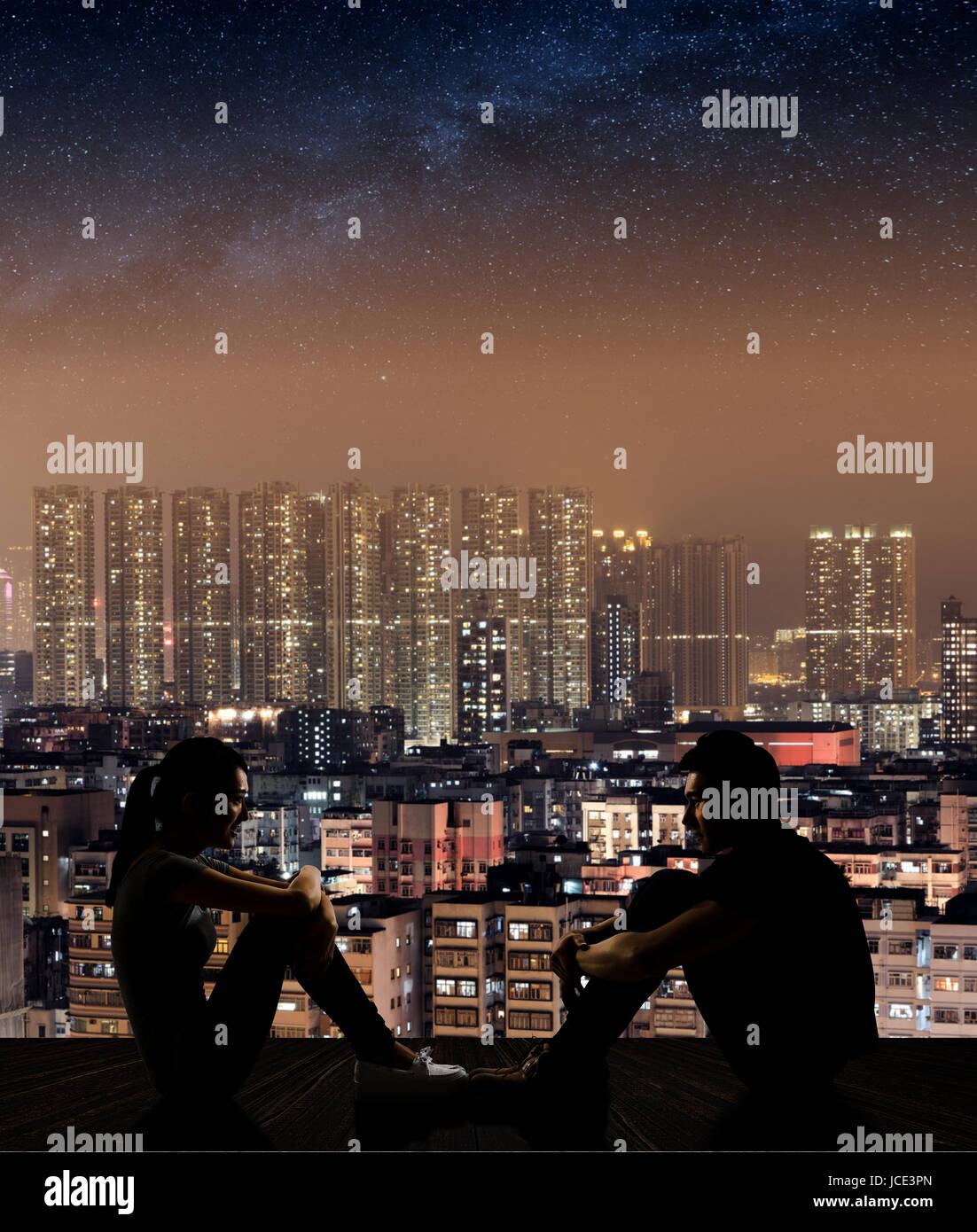 Silhouette of young couple face to face sit on ground in the city night ...