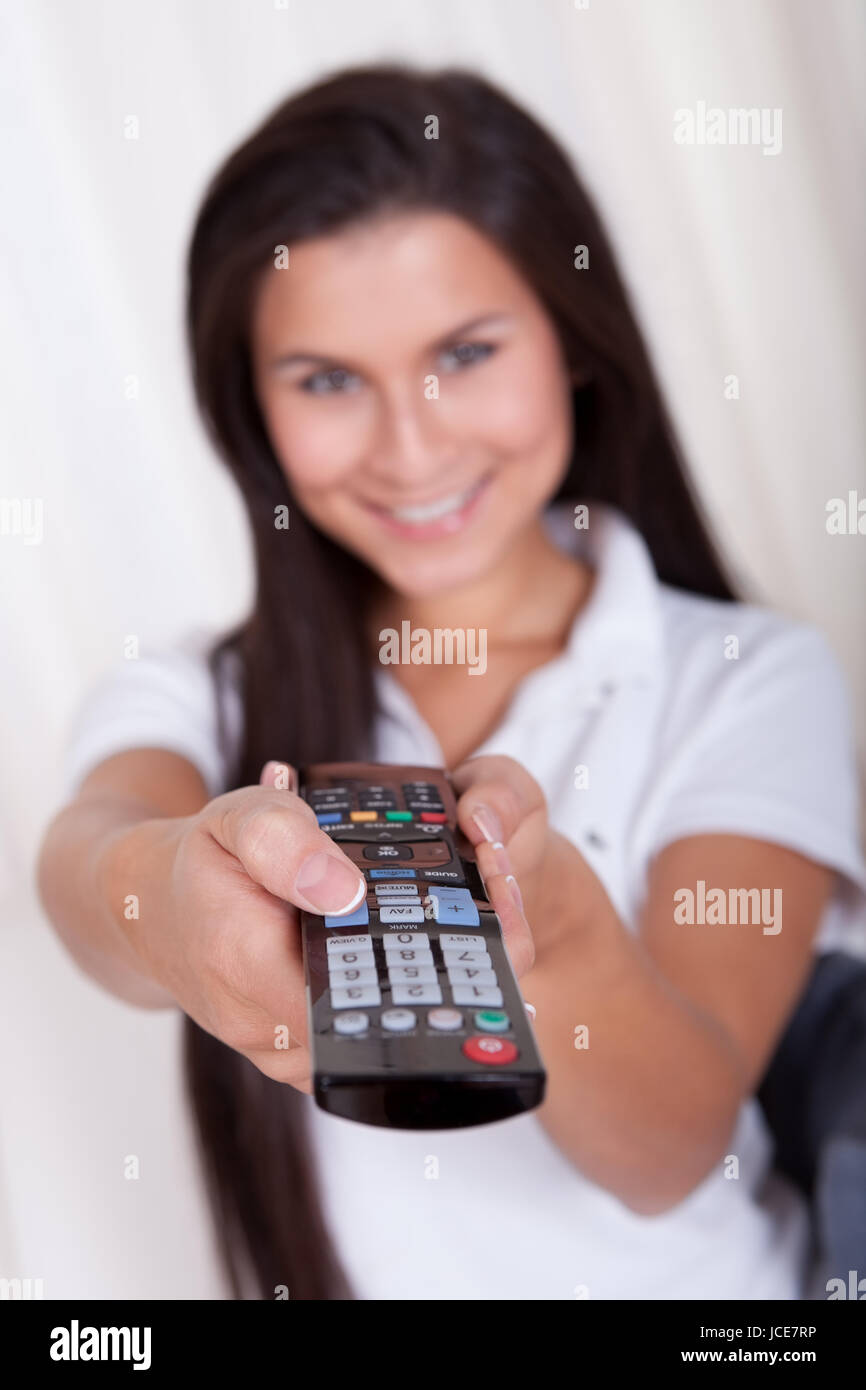 Smiling woman sitting on a couch with a remote control in her hands ...