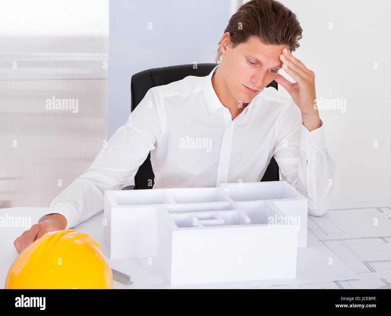 Frustrated Male Architect Sitting In Front Of Architectural Model In ...