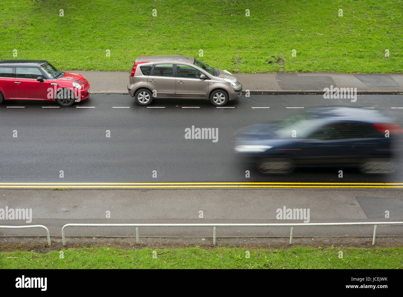 Cars parked in metered parking area on suburban road with passing ...
