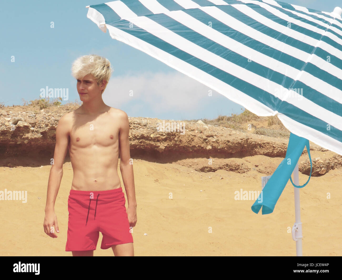 Boy on the beach with red bathing suit next to a blue and white striped ...