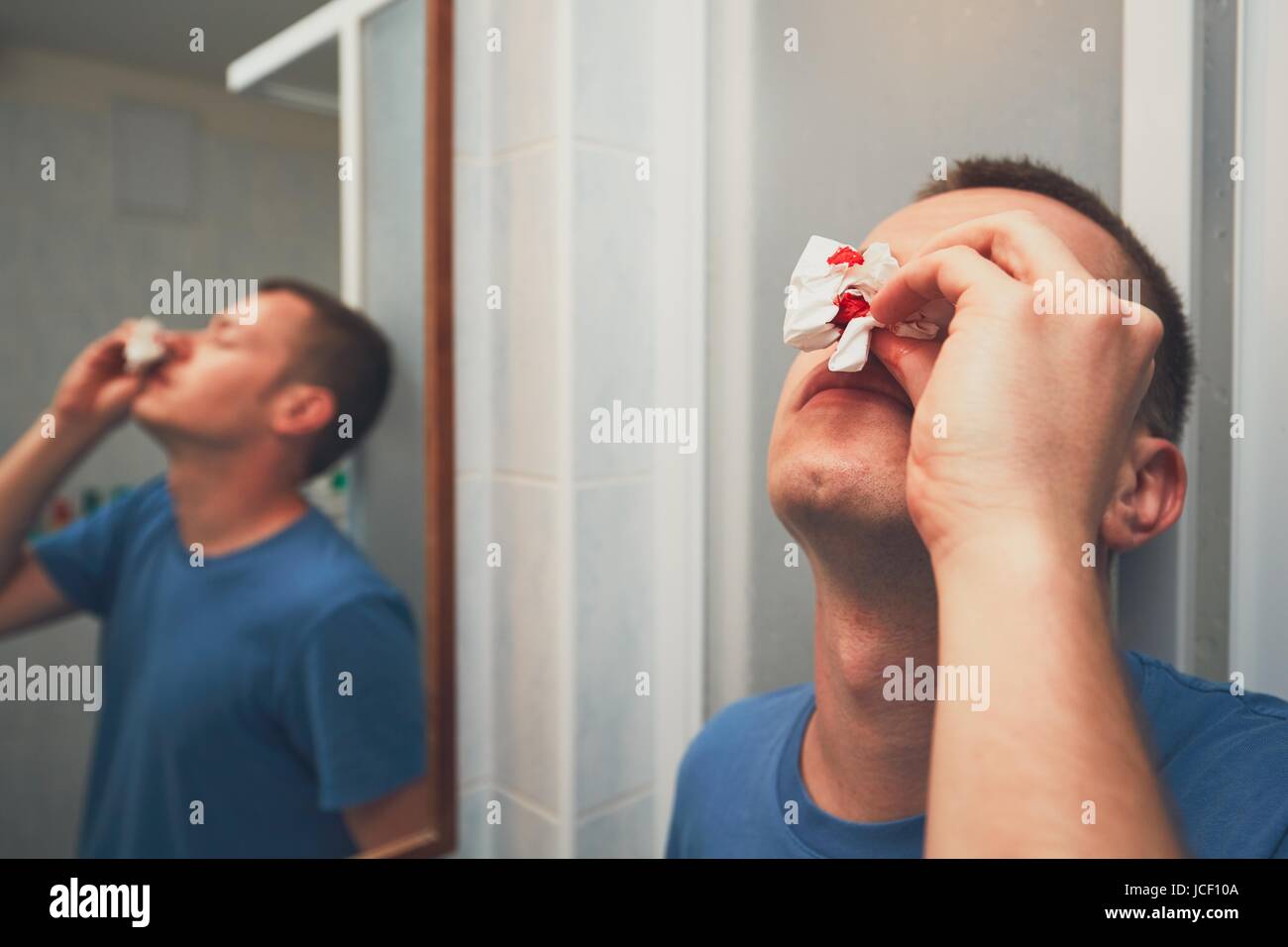Man with nose bleed in bathroom. For themes of illness, injury or ...