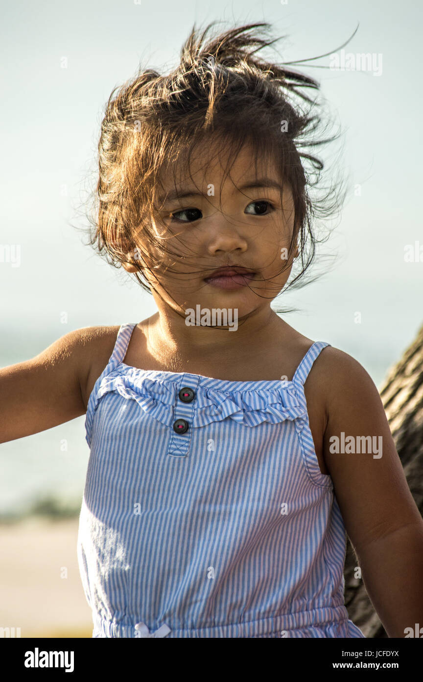 A little girl with wind tossed hair looks to her left with a slight ...