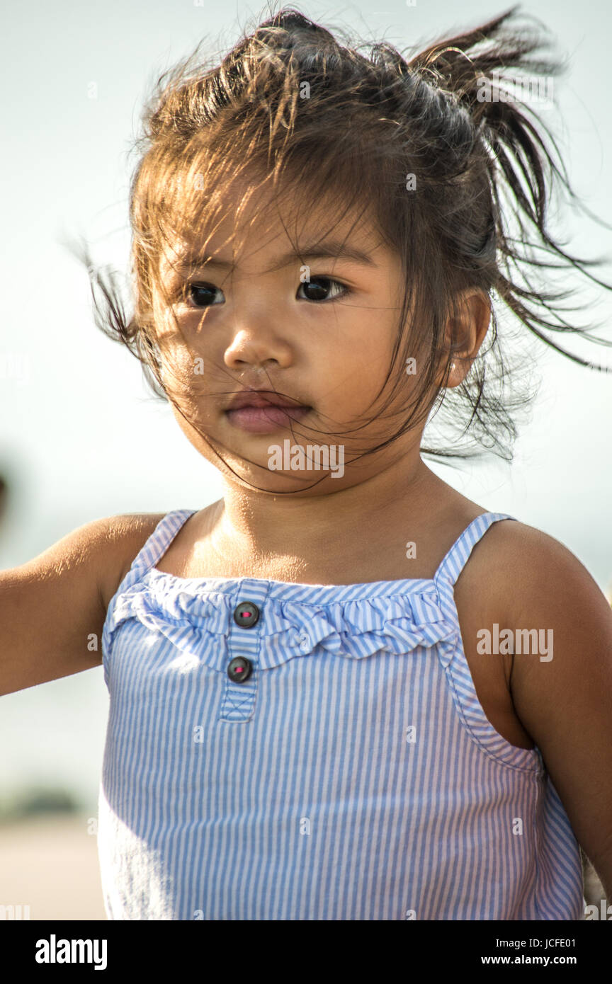 A young Pacific Isalnder girl with wind tossed hair looks intently in ...