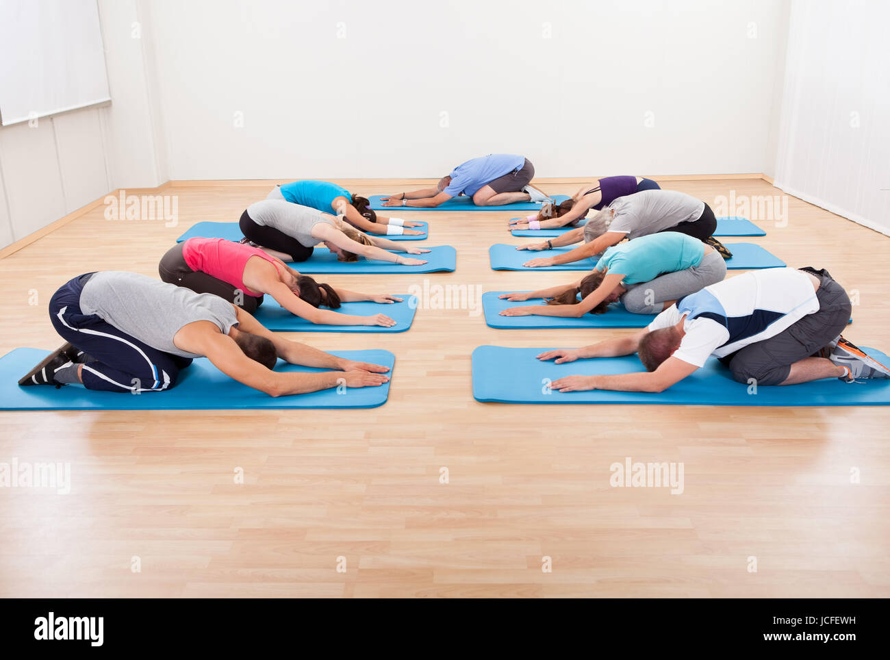 A mixed class of men and women stretching on individual floor mats in a ...