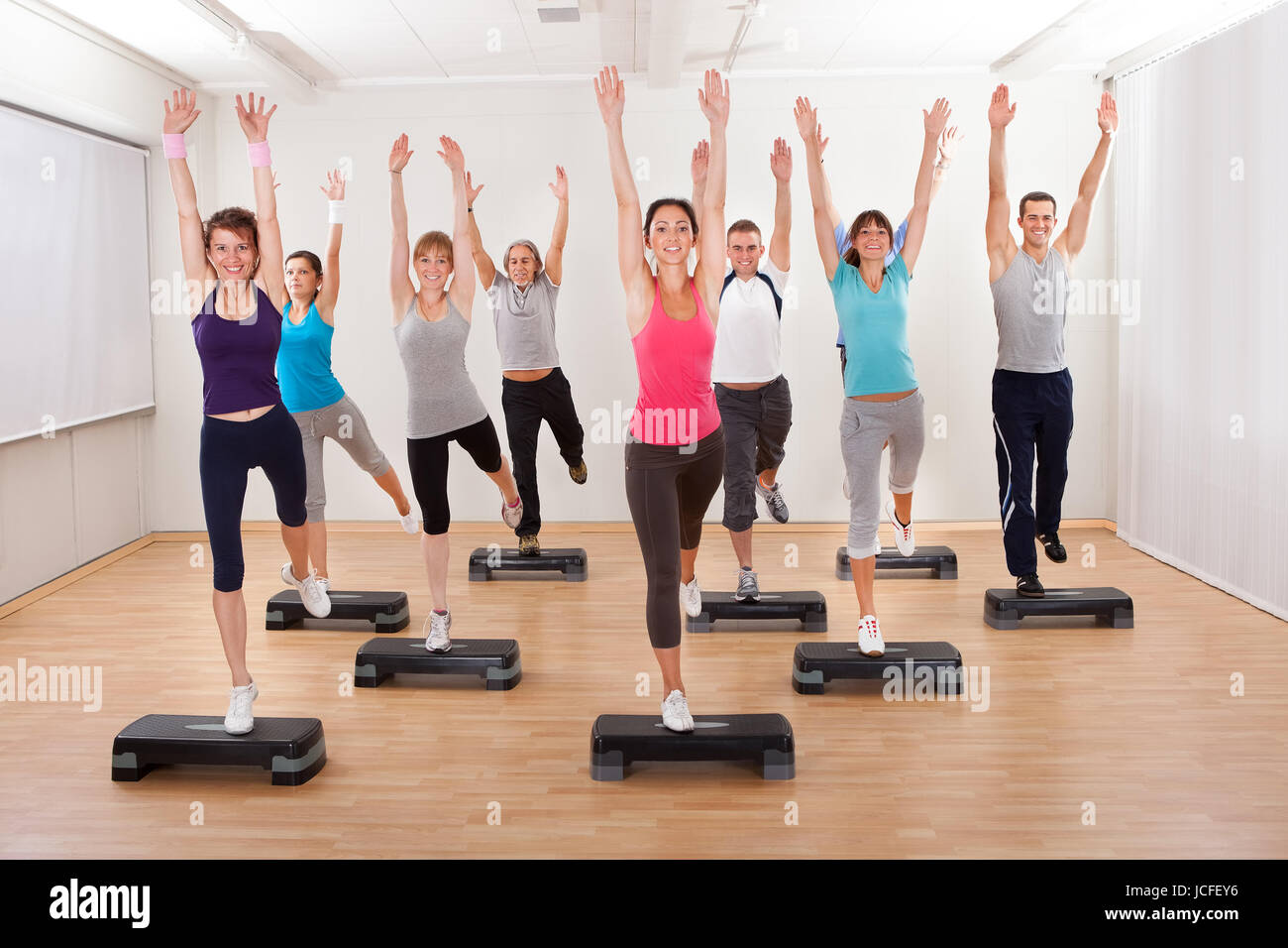 Diverse group of people in a class doing aerobics balancing on boards ...